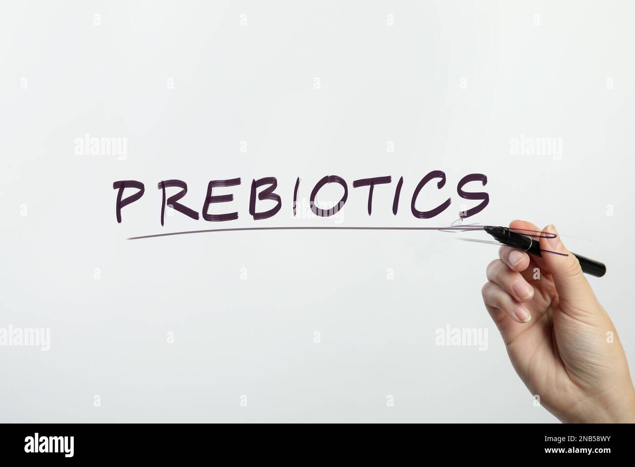 Woman writing word PREBIOTICS on glass against white background ...