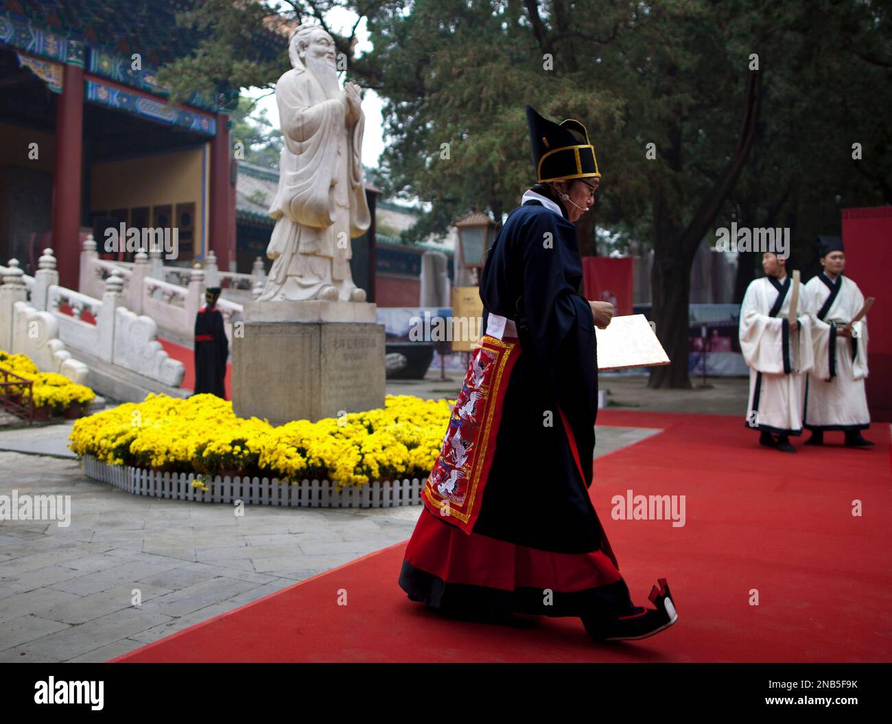 A Chinese dressed as an ancient Chinese scholar walks past a statue of ...