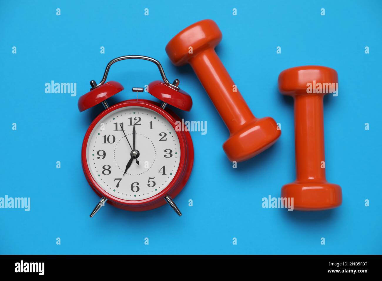 Alarm clock and dumbbells on light blue background, flat lay. Morning ...