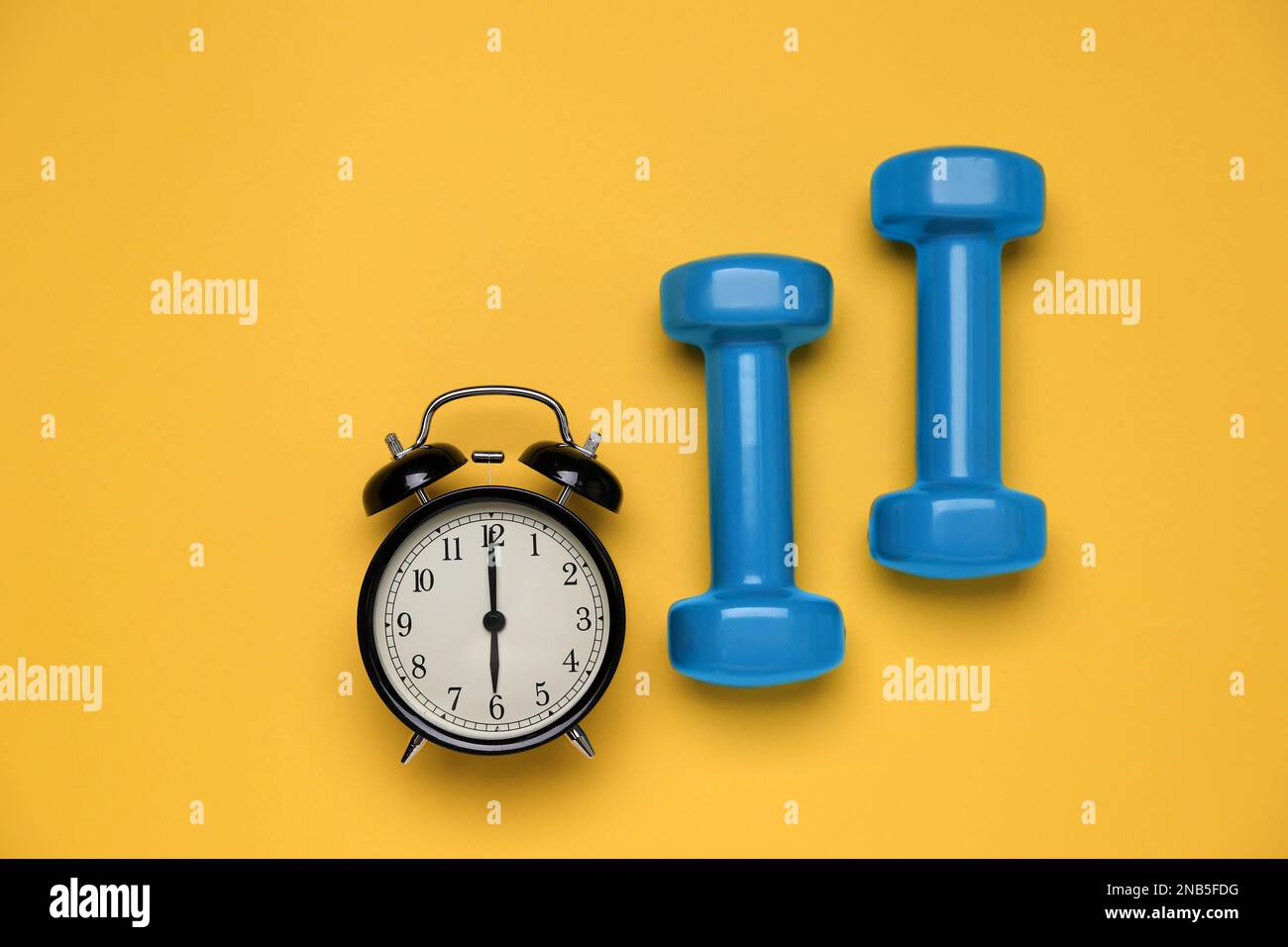 Alarm clock and dumbbells on yellow background, flat lay. Morning ...