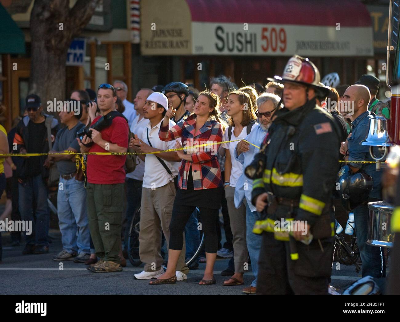 A crowd of onlookers watch as San Francisco firefighters work on top of ...