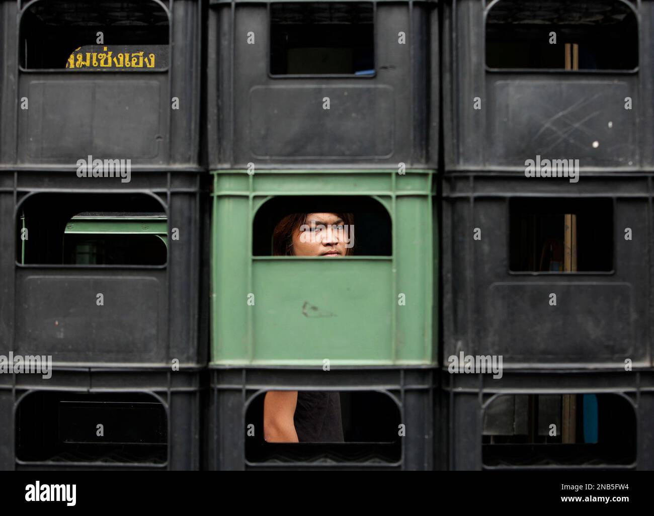 A Thai worker stands behind plastic boxes in Bangkok, Thailand ...