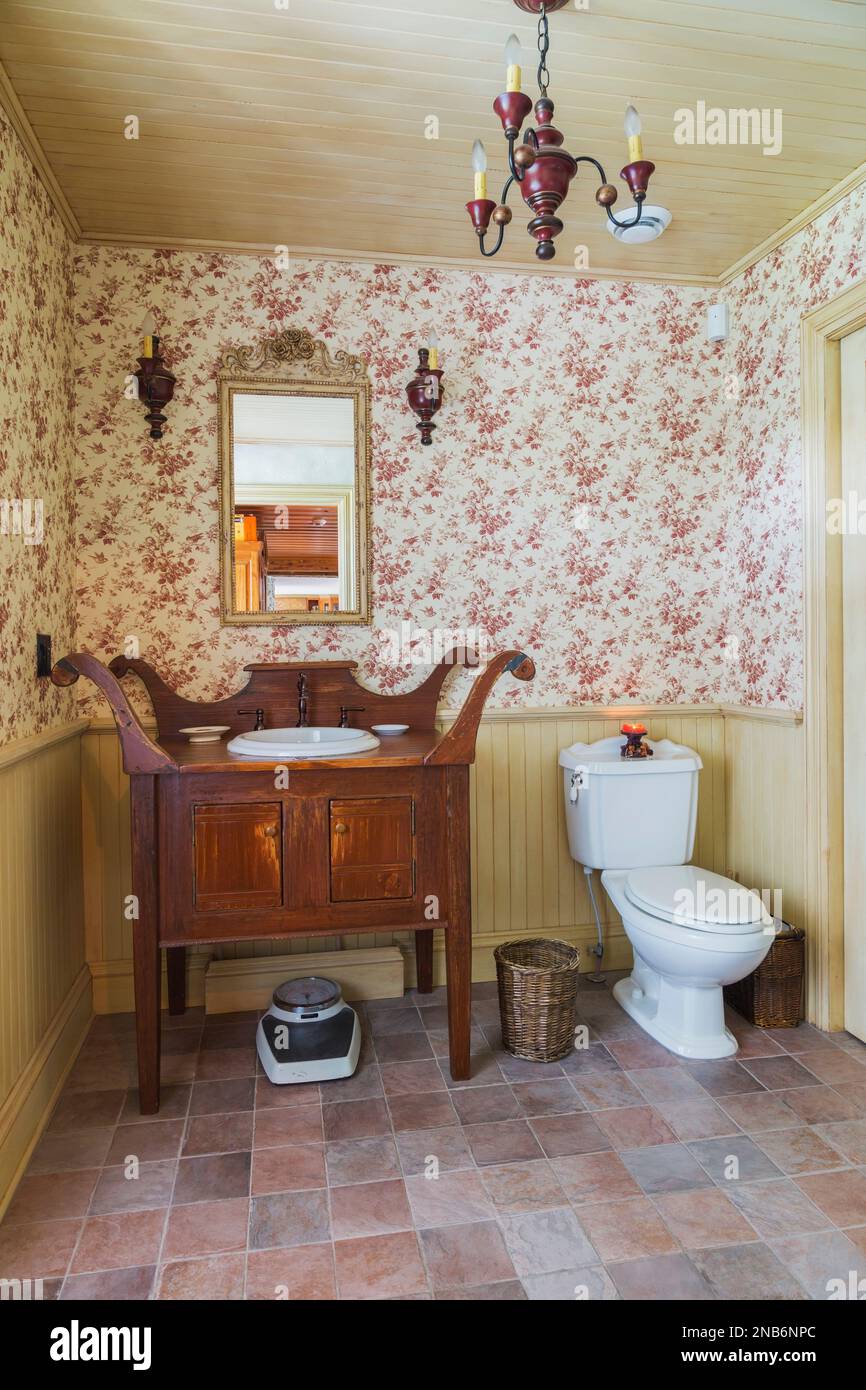 Antique wooden vanity and white porcelain toilet in guest washroom with ...