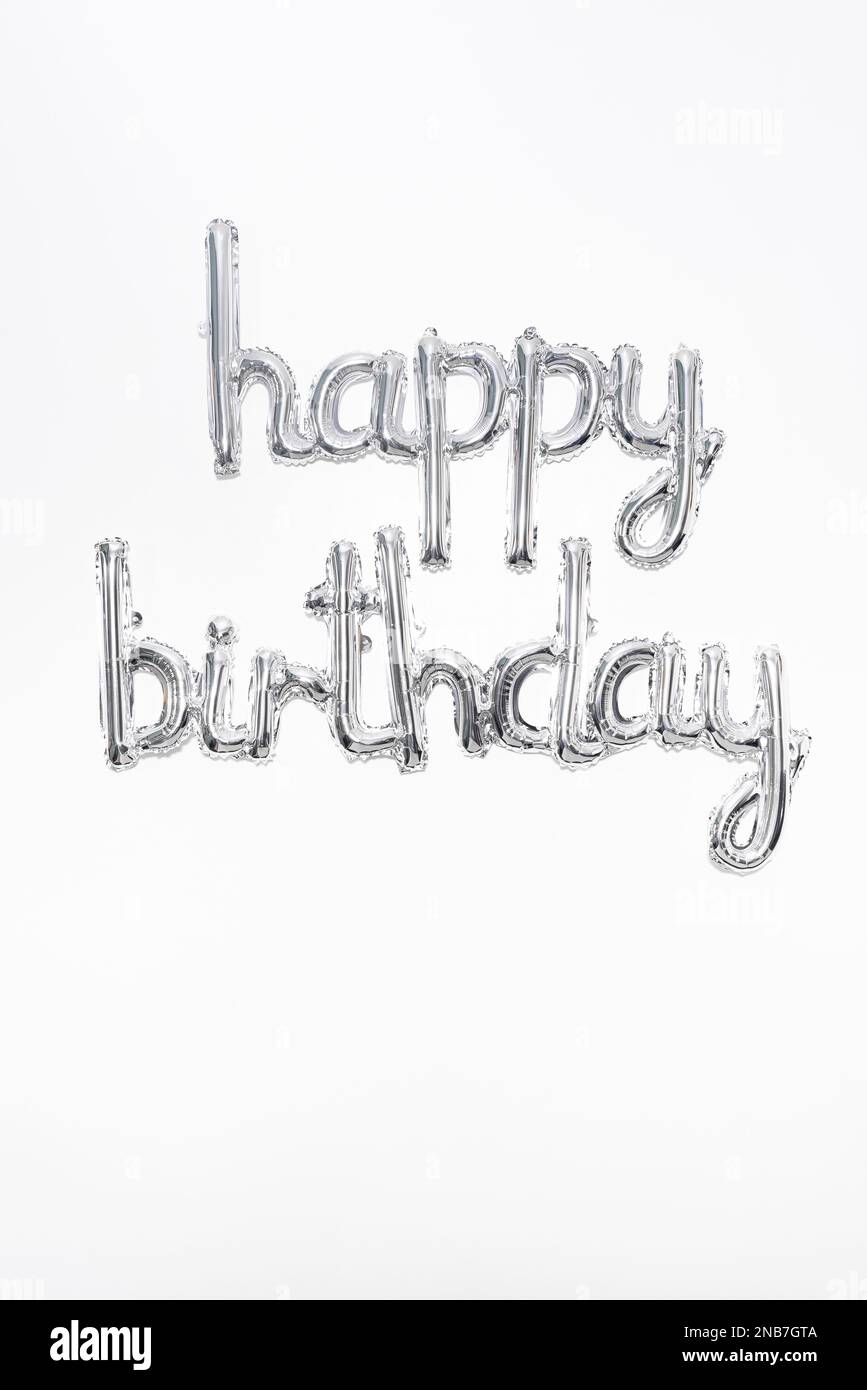 Silver happy birthday balloon lettering on a white wall. Foil letters ...