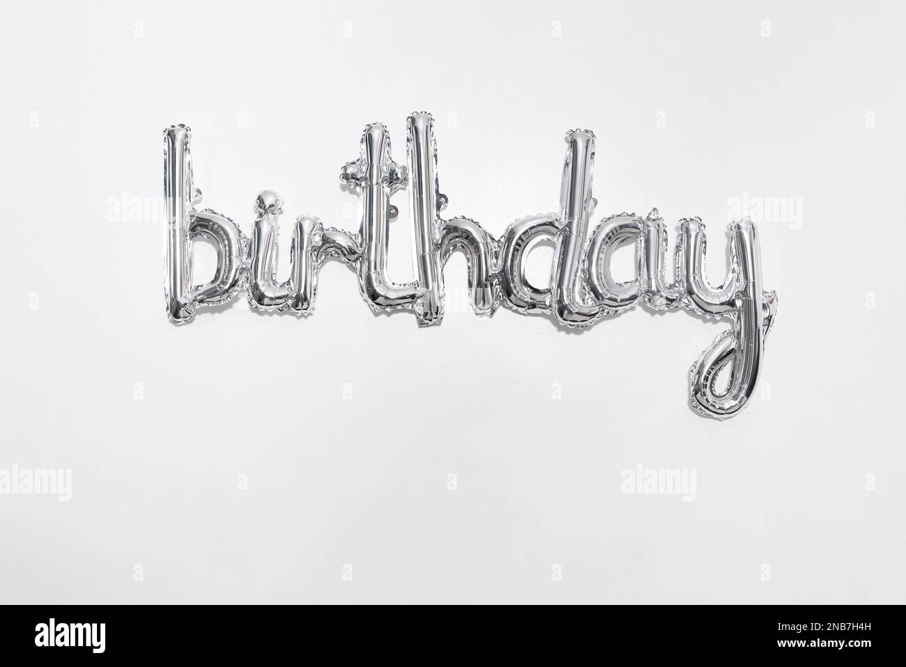 Silver birthday balloon lettering center on a white wall. Foil letters ...