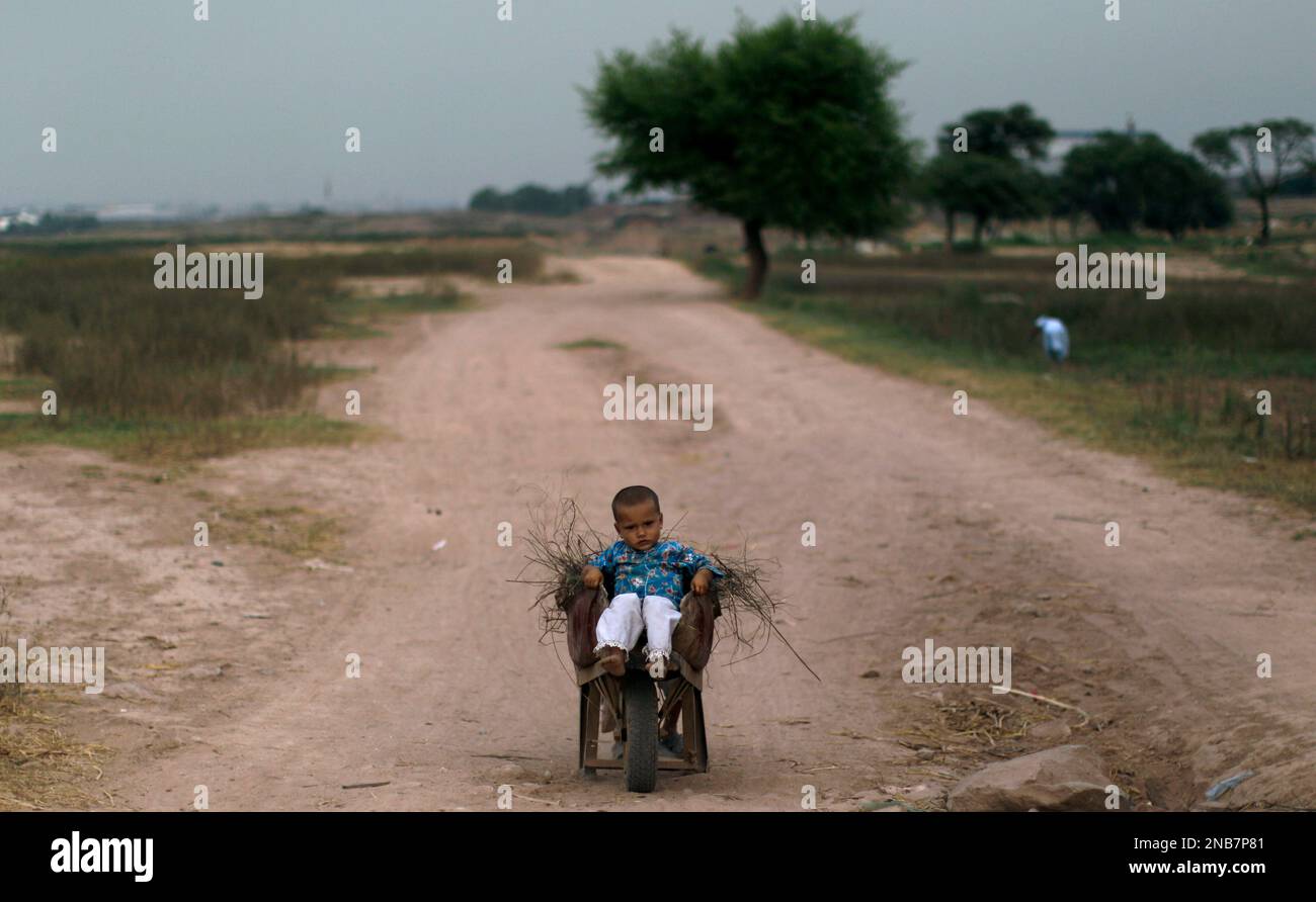 A Pakistani child, sitting in a wheelbarrow loaded with wood, looks on ...