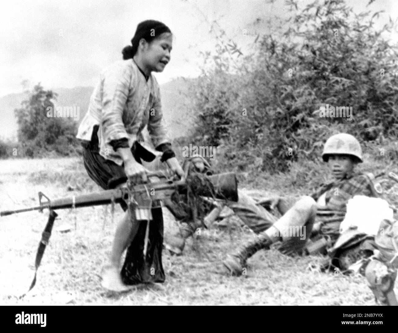 A peasant woman carries a muddy M-16 rifle to a group of wounded South ...