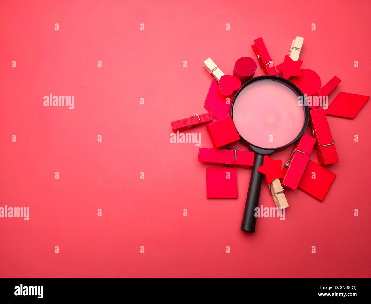 Magnifying glass and colored wooden clips on a red background with copy ...