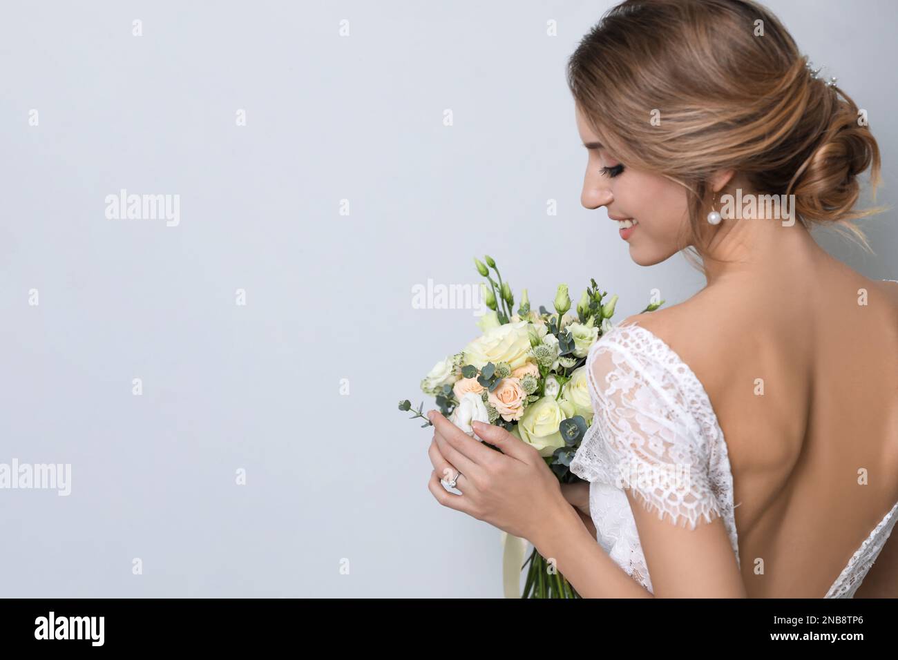 Young bride with beautiful wedding bouquet on light grey background ...