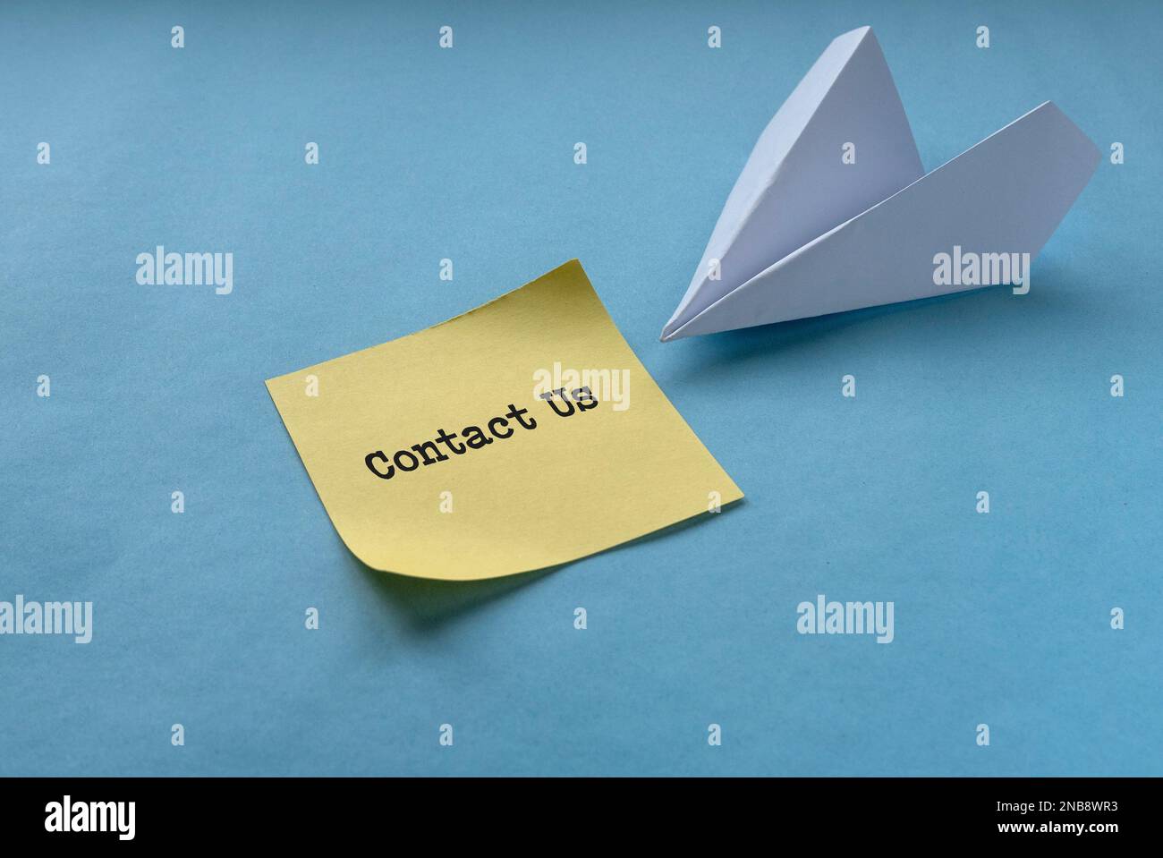 Contact us concept written on yellow memo note with paper plane on blue ...