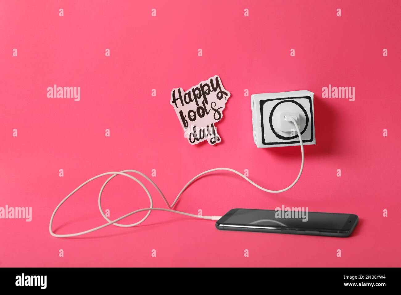 Mobile phone connected to fake plug and words Happy Fool's Day on pink ...
