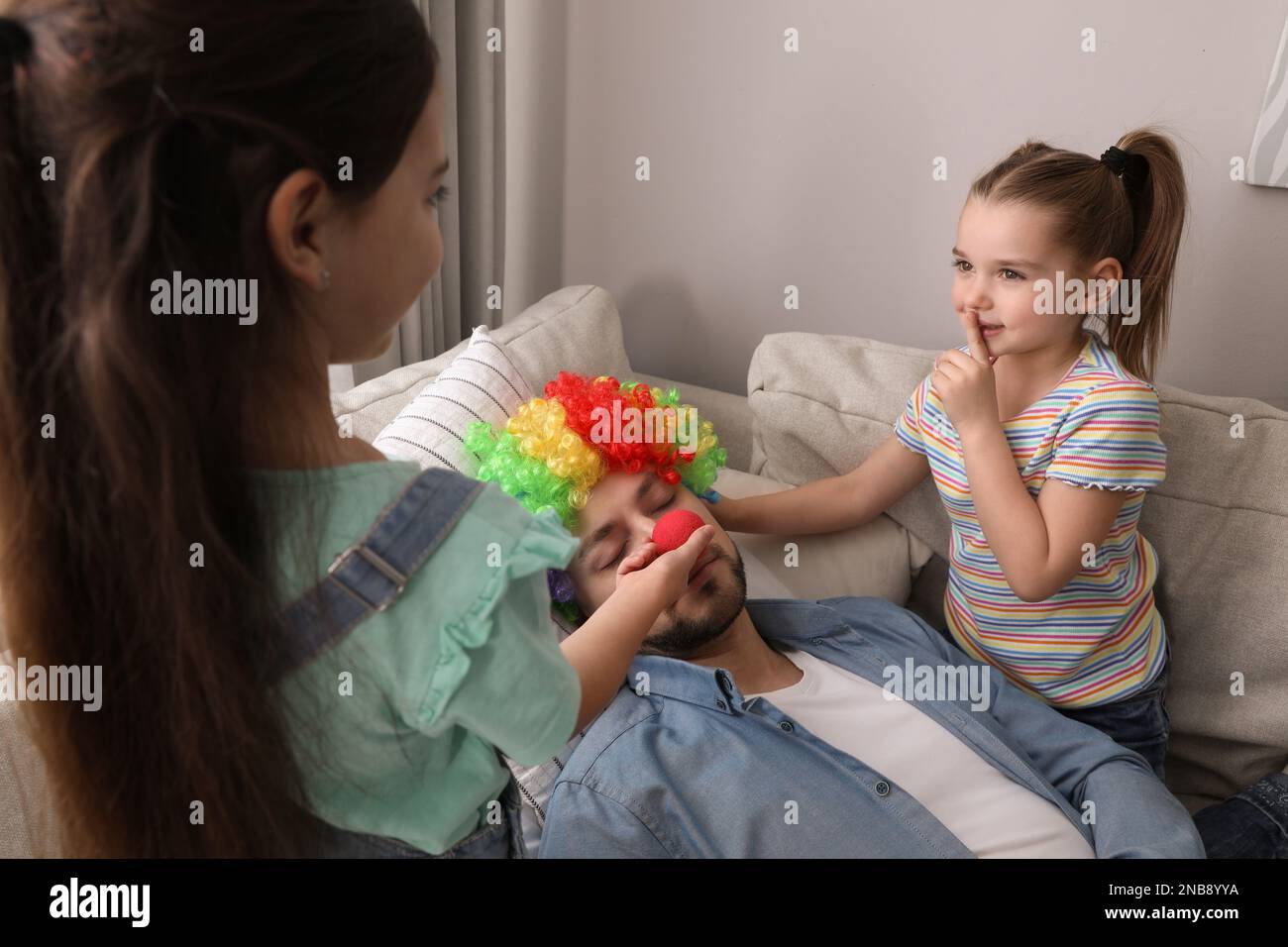 Cute little children putting clown nose and wig on father while he ...