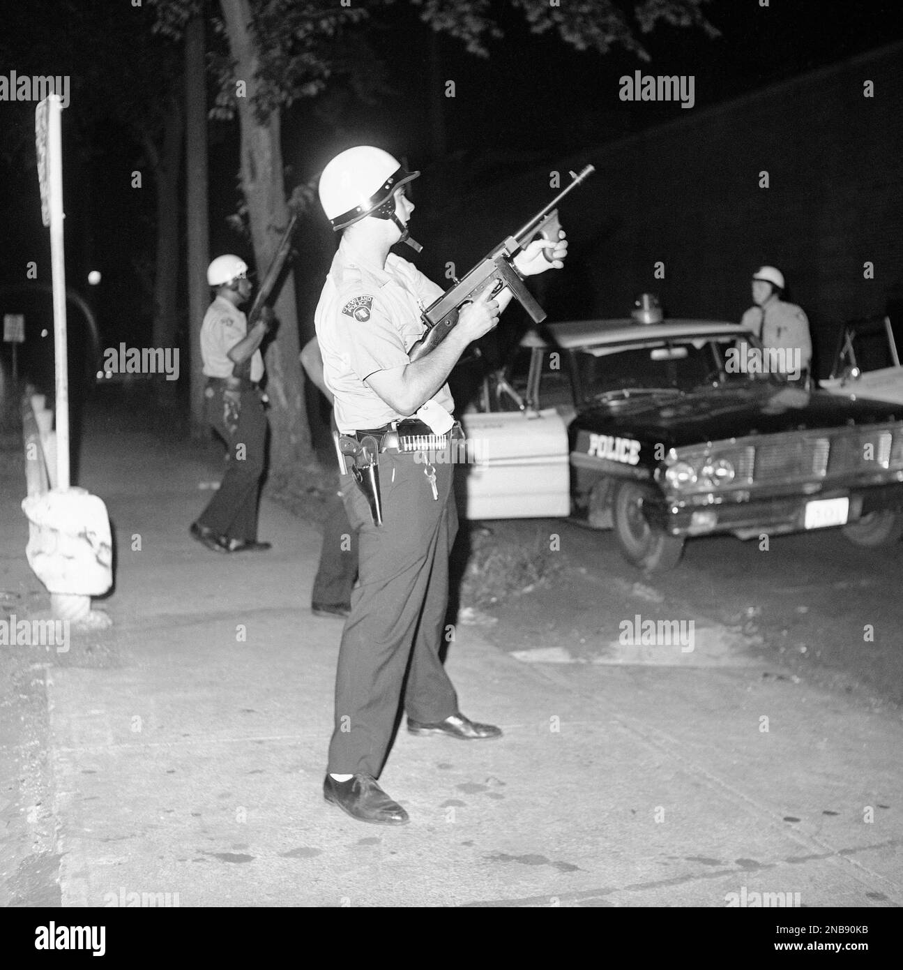 A police officer aims a Tommy gun toward the roof of a theater in the ...