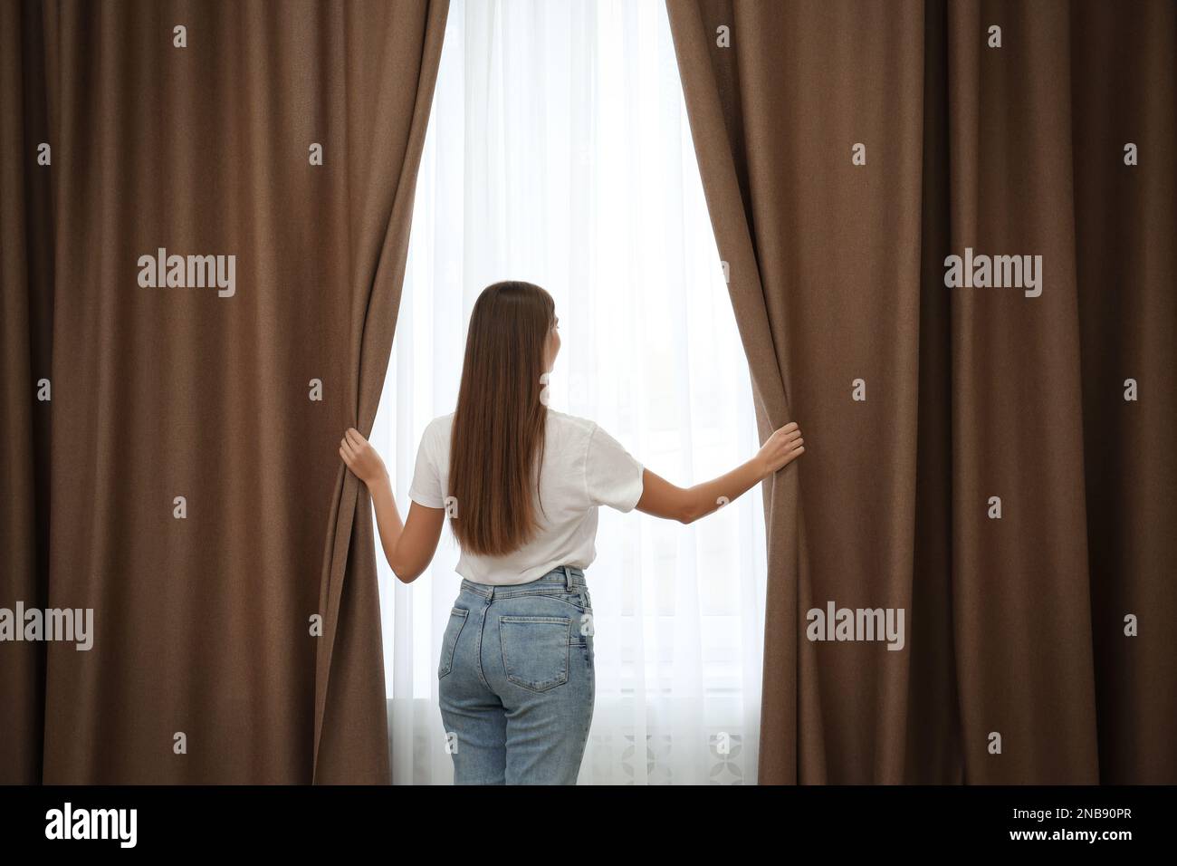 Woman opening elegant window curtains in room, back view Stock Photo ...