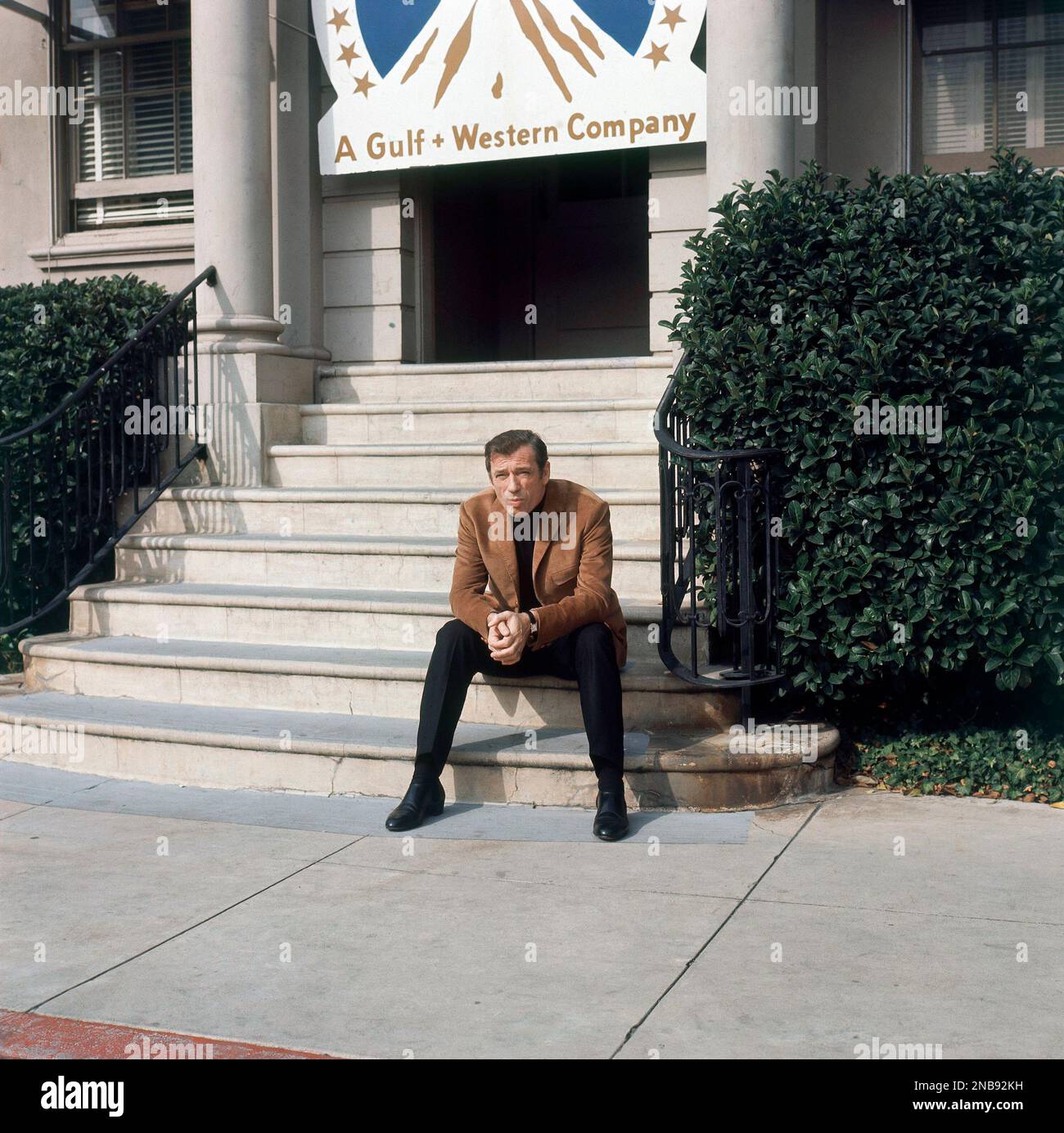 Yves Montand sits on the steps in front of Paramount Pictures' offices ...