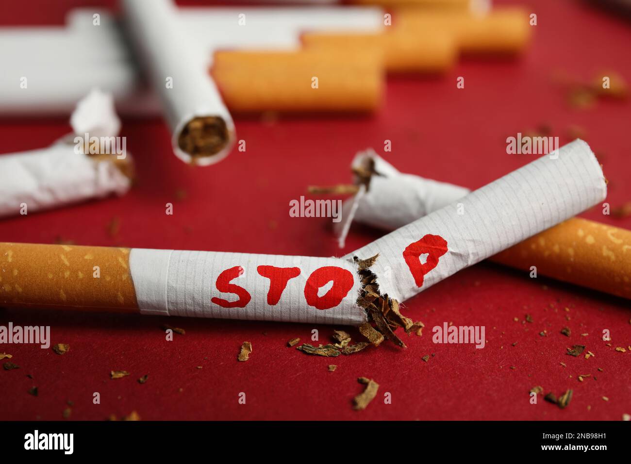 Broken cigarette with word Stop on red background, closeup. Quitting ...