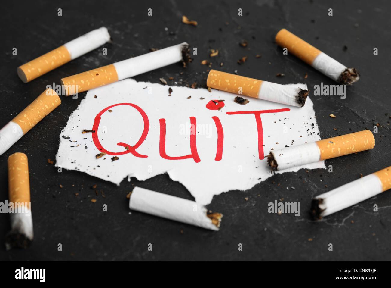 Cigarette stubs and paper with word Quit on black slate table. Giving ...