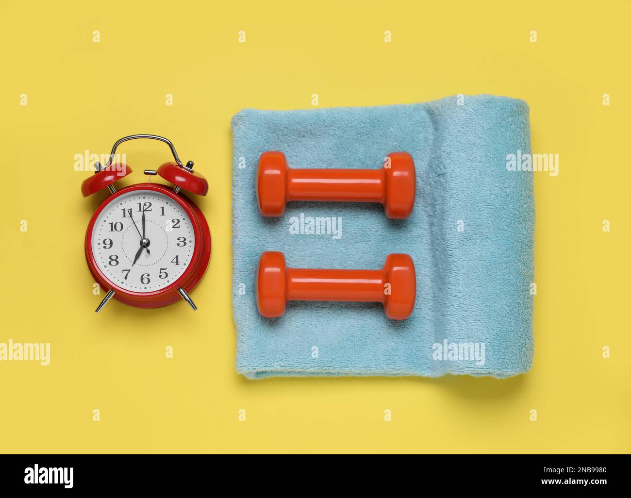 Alarm clock, towel and dumbbells on yellow background, flat lay ...