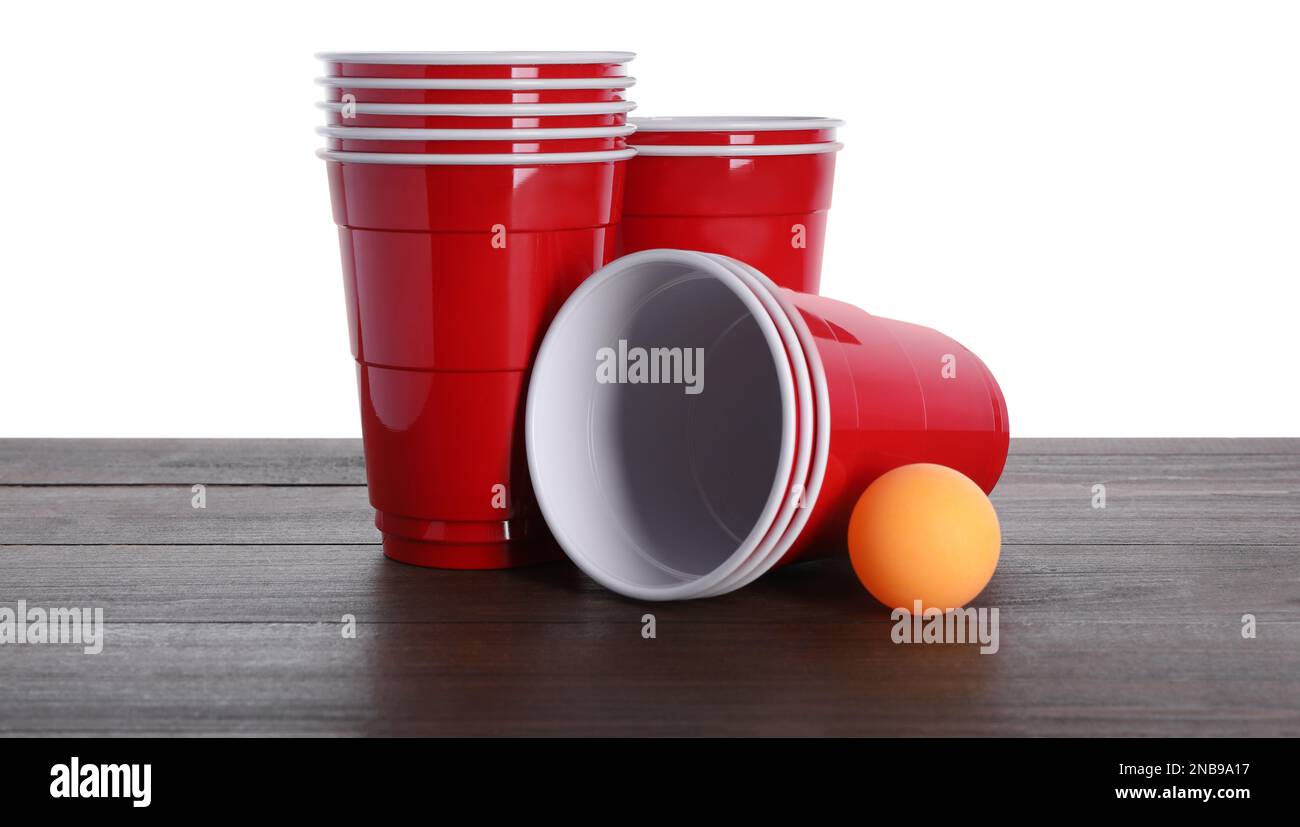 Plastic cups and ball for beer pong on wooden table against white ...