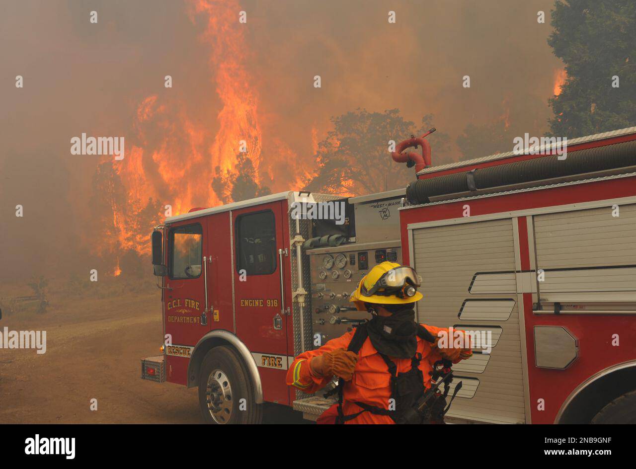A firefighter puts on gear as a large wildfire to the southwest of ...