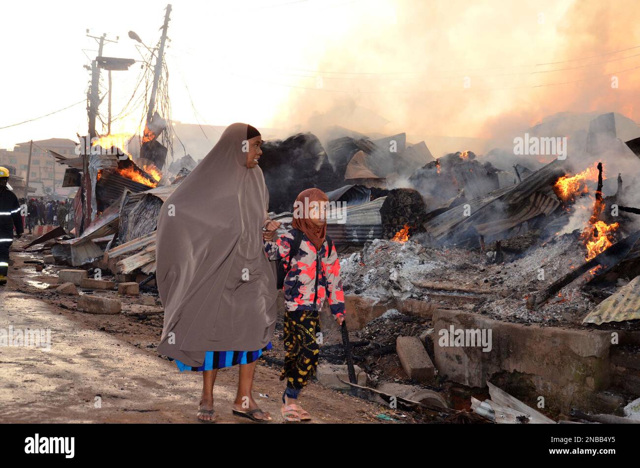 Kampala. 13th Feb, 2023. A woman and her child walk past a fire burning ...