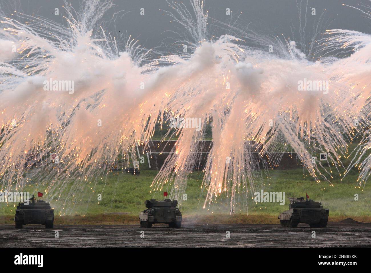 A line of Japan Ground Self-Defense Force tanks flare up a smoke screen ...