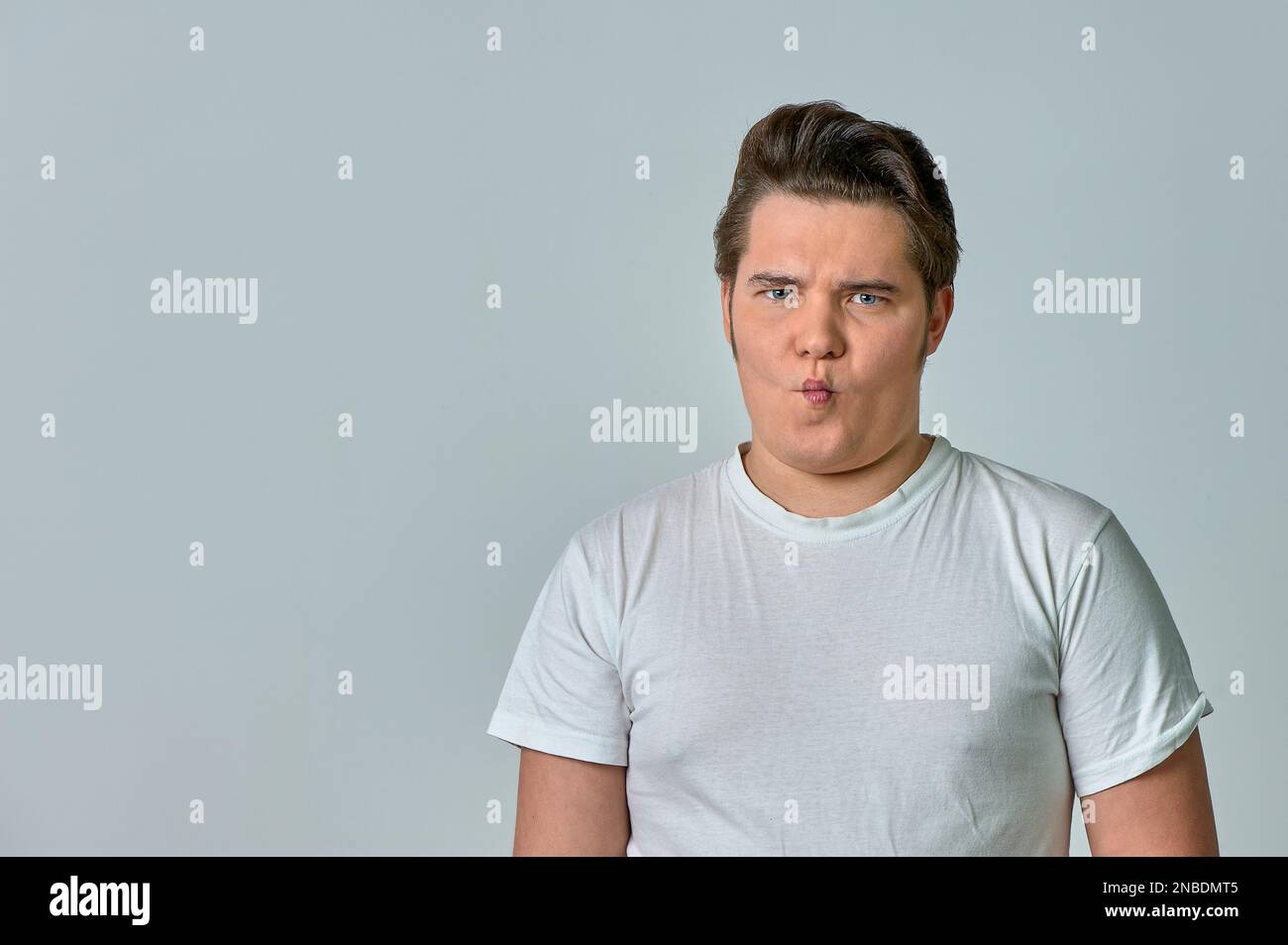a man puffing out his cheeks with a funny face on a gray background ...