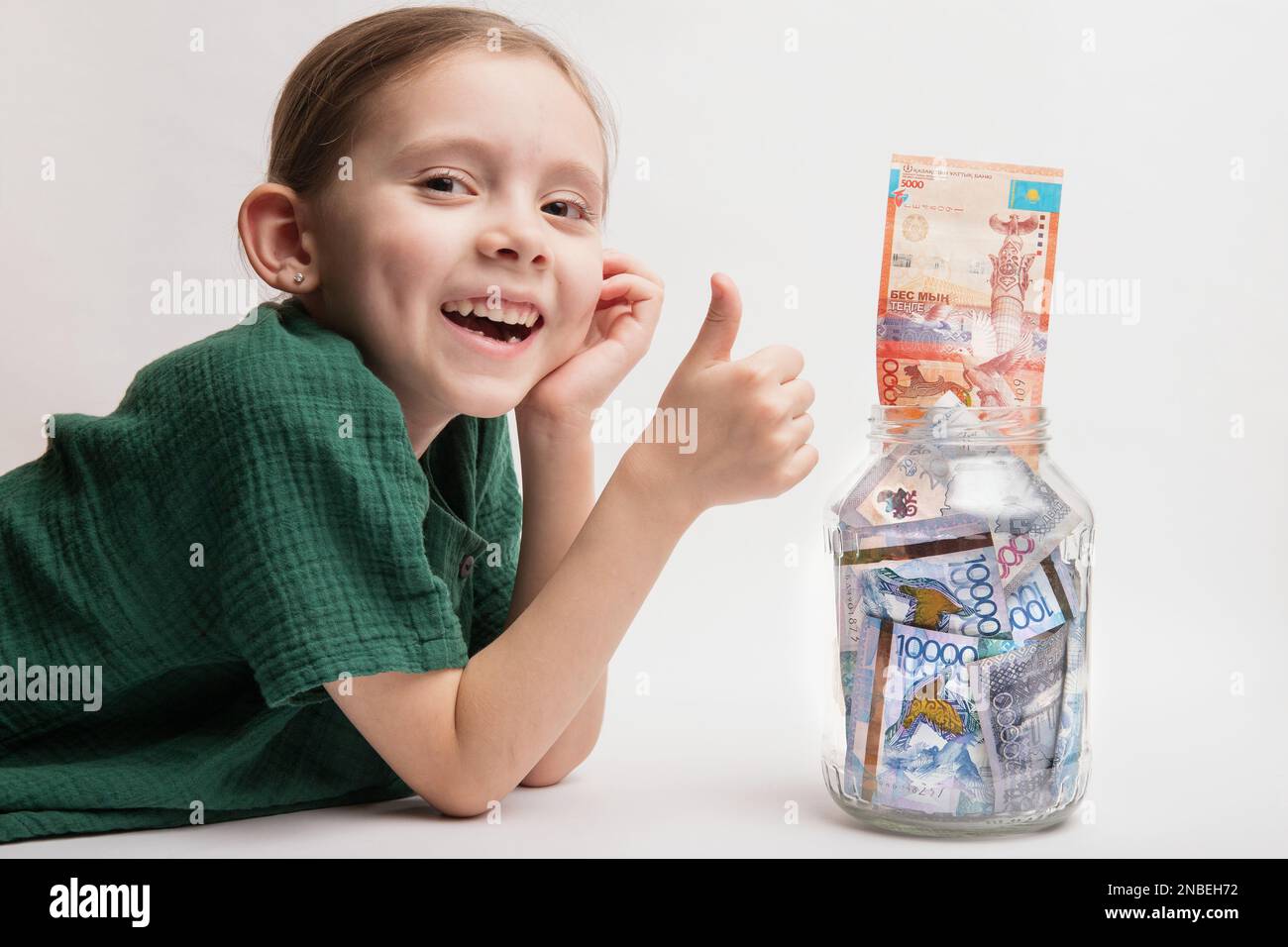 Kid with a large transparent jar with Kazakhstani tenge money. Bank ...