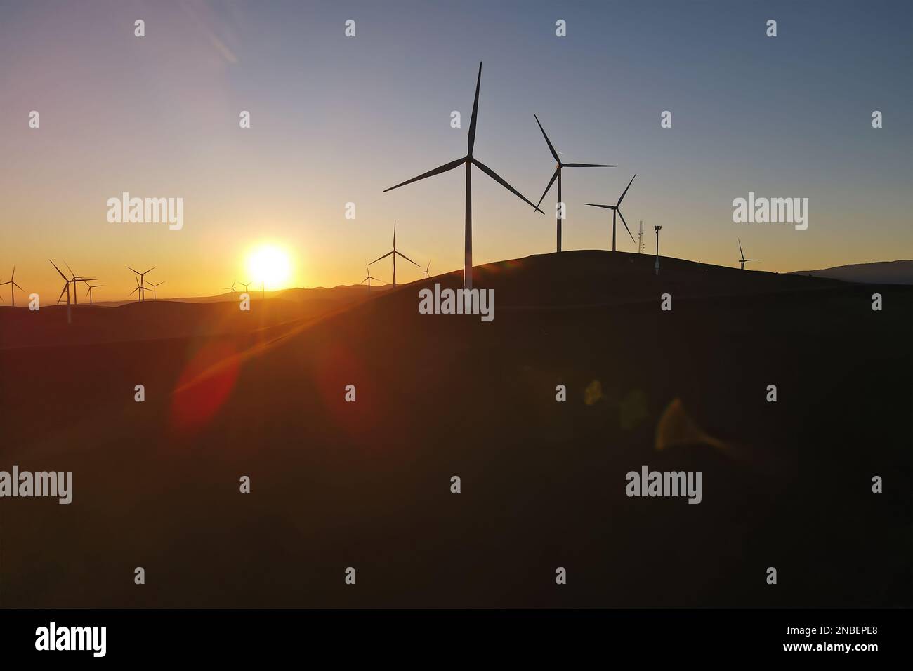 Wind power turbines on the hill in a sunset or sunrise light ...