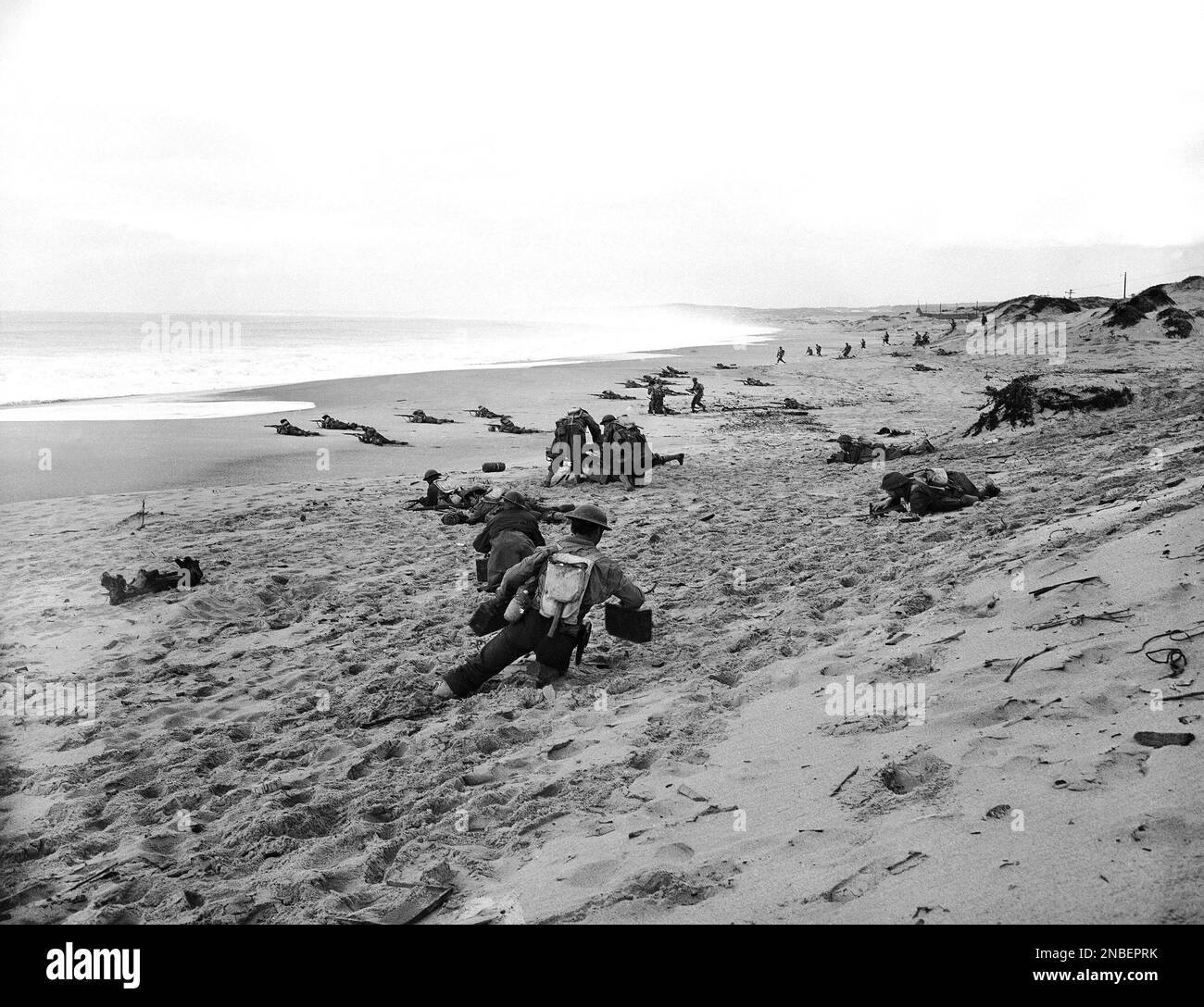 These infantrymen armed with machine guns and automatic rifles maneuver on beach in California ...