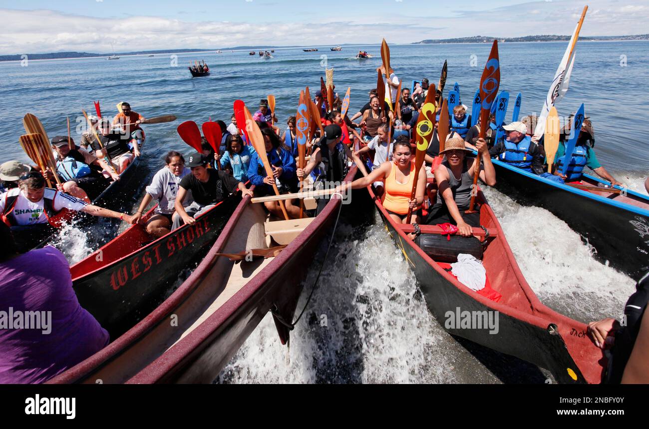 Tribal canoes are rocked by waves as they raft together near shore ...