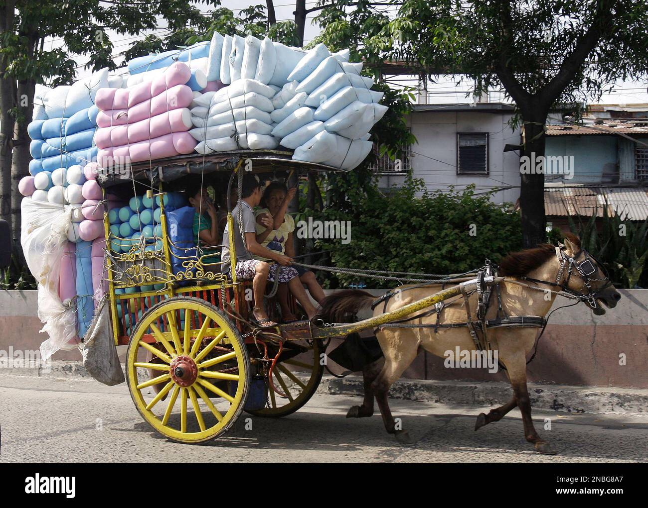 Filipinos ride a horse-drawn carriage loaded with pillow cases along a ...