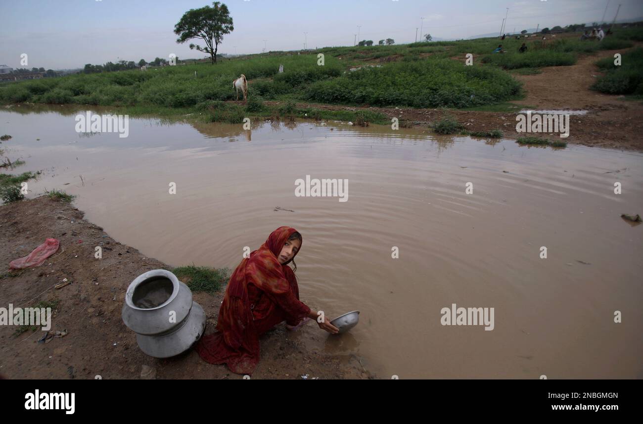 A Pakistani girl cleans her family's bowls in a ditch full of rain ...