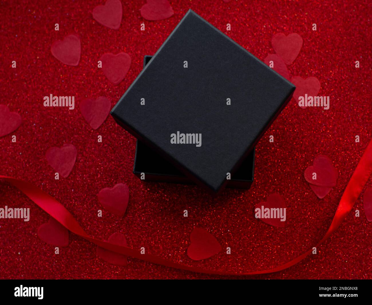 Black gift box is on red heart paper background, top view. Greeting ...