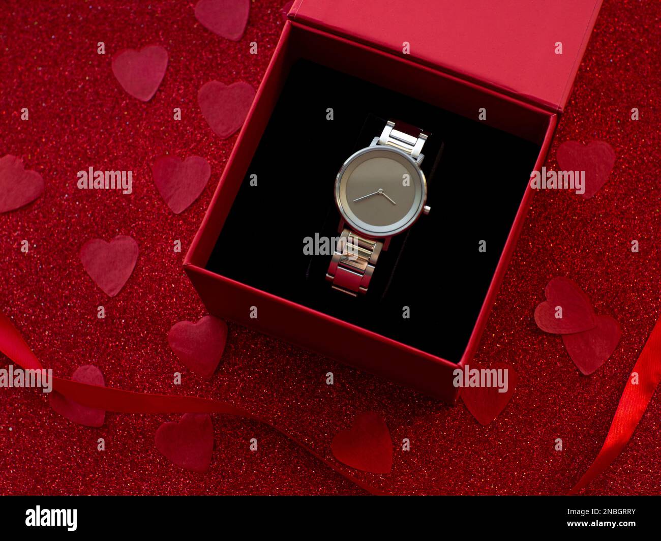 Gift box with silver watch is on red heart paper background, top view ...