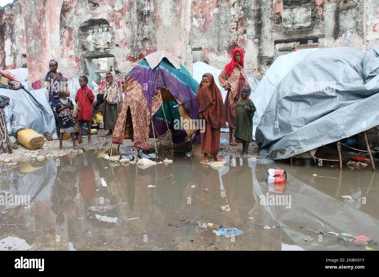 Somali families from southern Somalia stand around a pool of rain water ...
