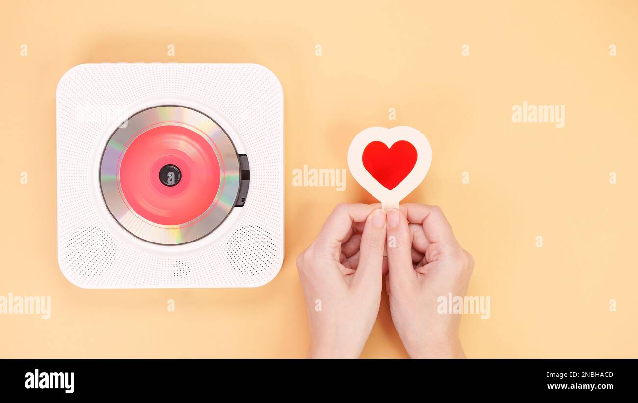 Hands holding heart shape red gift card next to white cd player with ...