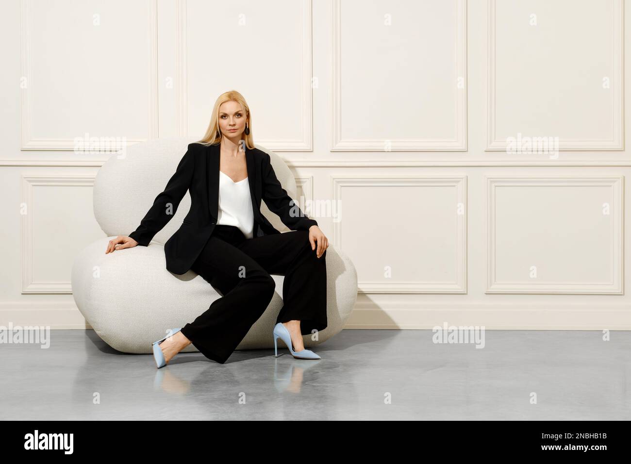 Cute woman in black jacket and wide trousers sitting in the room Stock ...