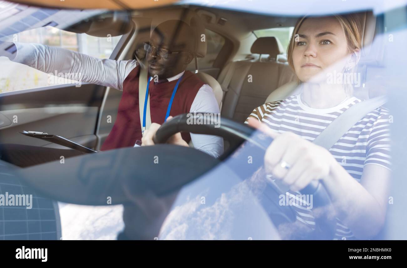 Driving school concept. A car instructor teaches a young woman how to ...