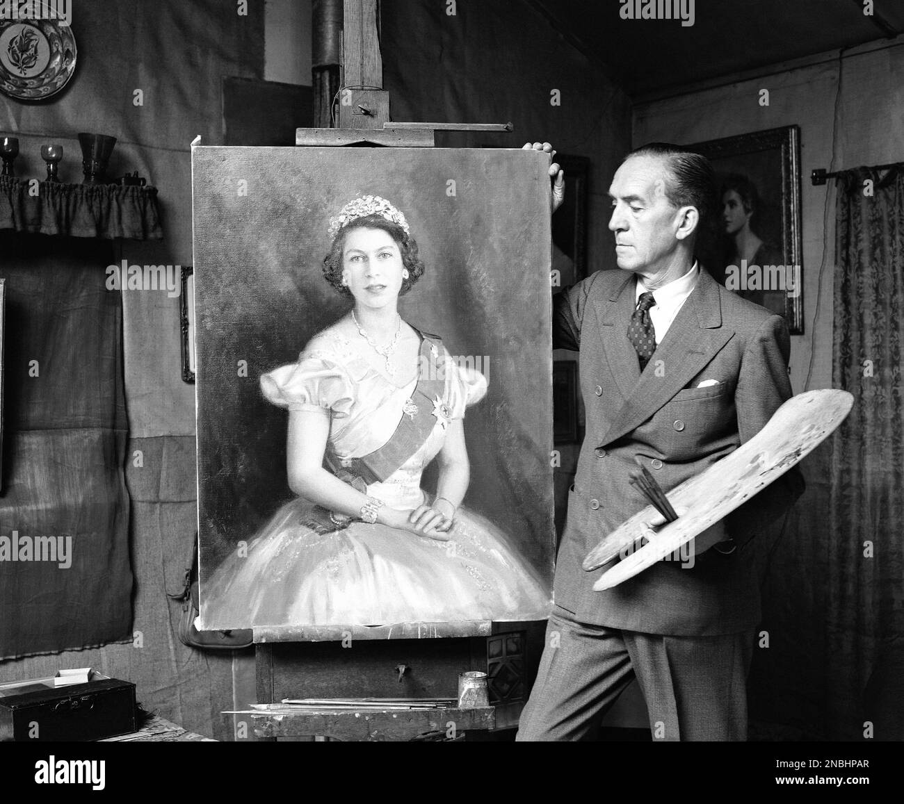 Commander Denis Fildes, holding brushes and a palette, looks at a ...