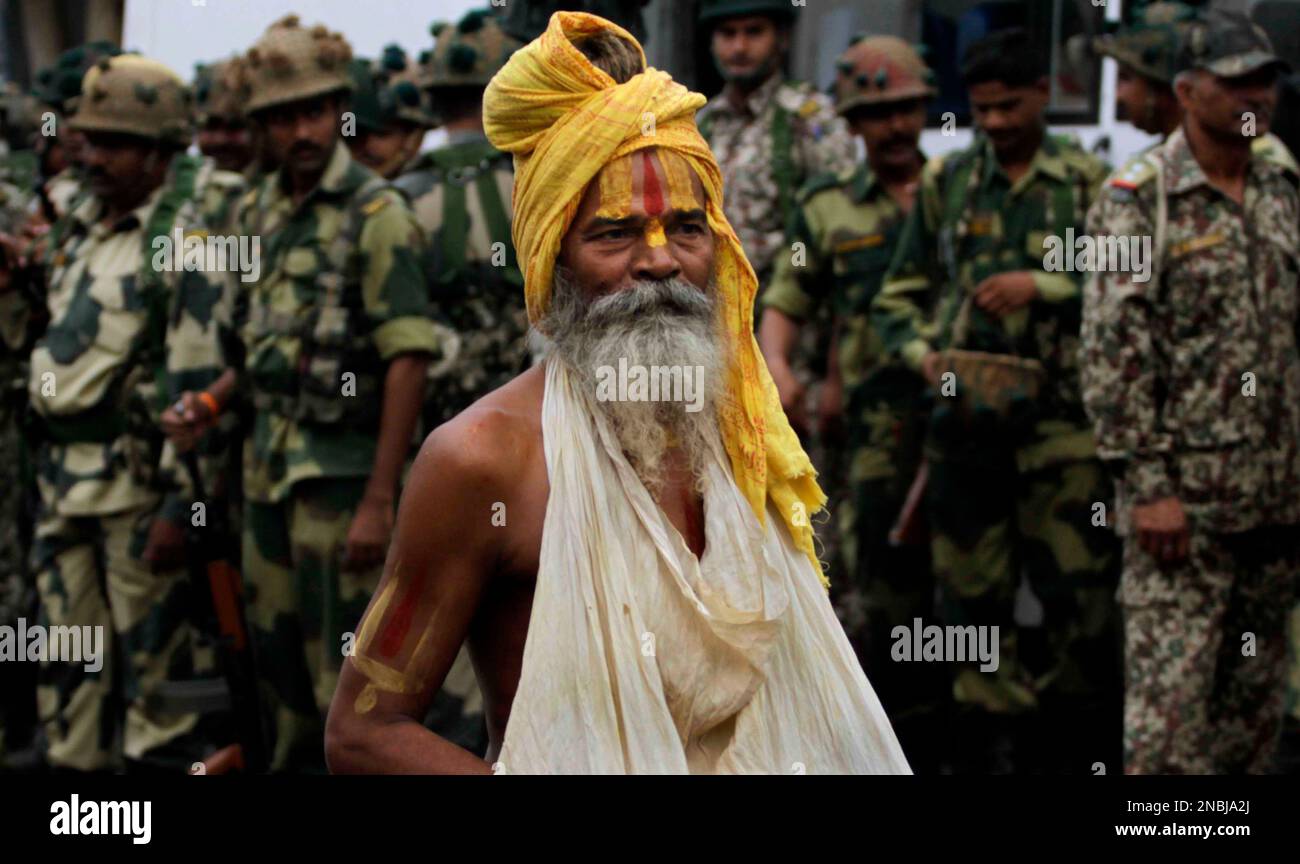 An Indian Hindu holy man walks past paramilitary soldiers performing a ...