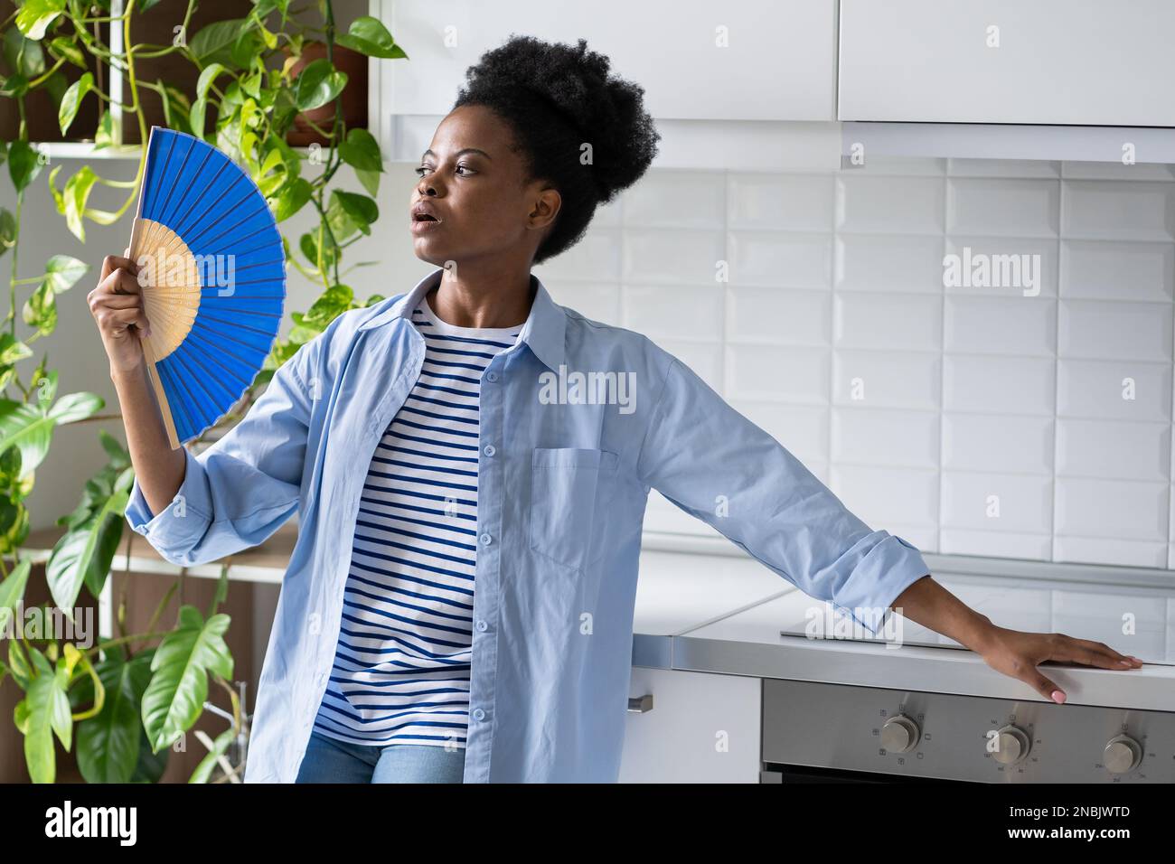 Young African American woman in blue shirt fanning herself with hand ...
