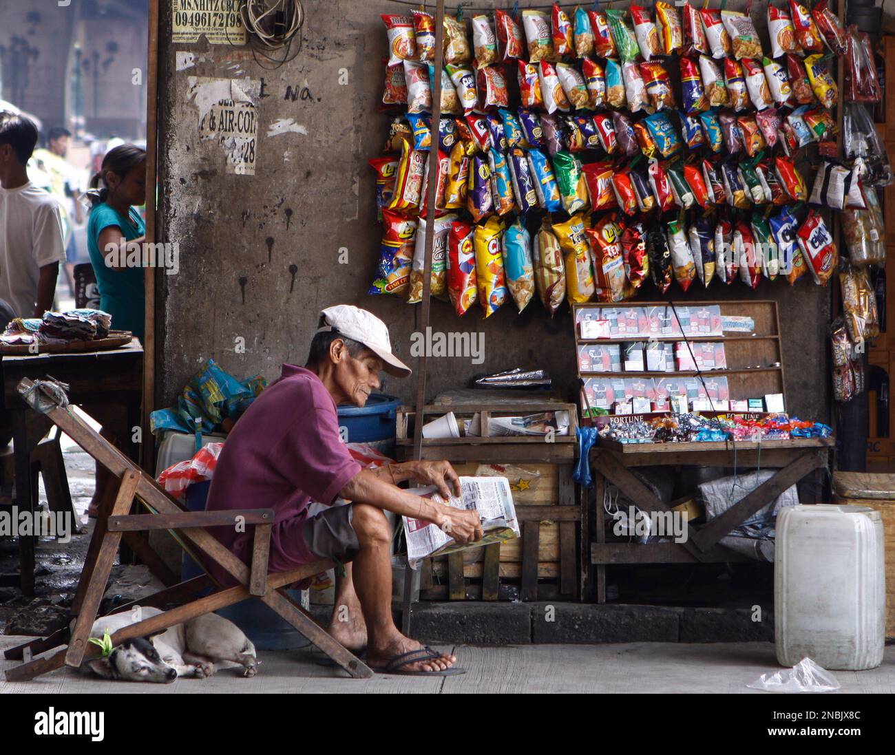 A Filipino man reads a newspaper beside his makeshift store along a ...