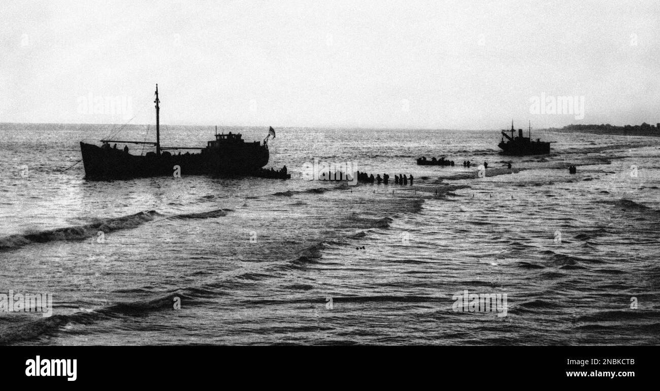 Men are wading through shallow water along the beach at Dunkirk on June ...