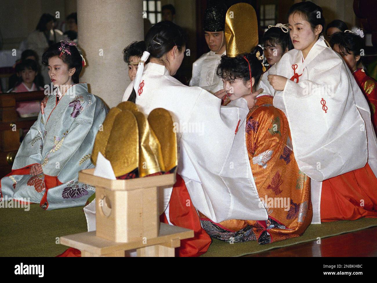 Maids in traditional court attire adjust a gold colored crown on a ...