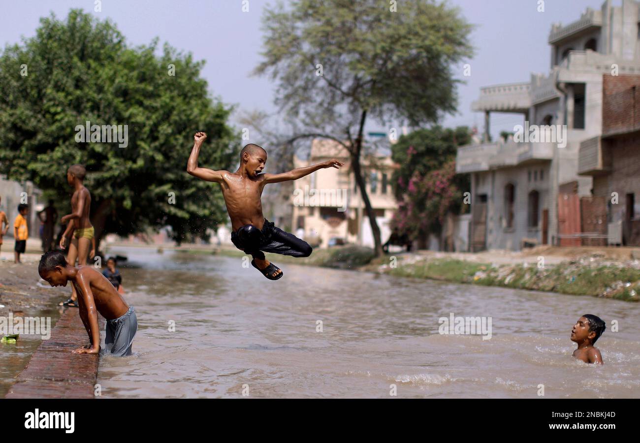 A Pakistani boy leaps into a watercourse, as he and other children cool ...