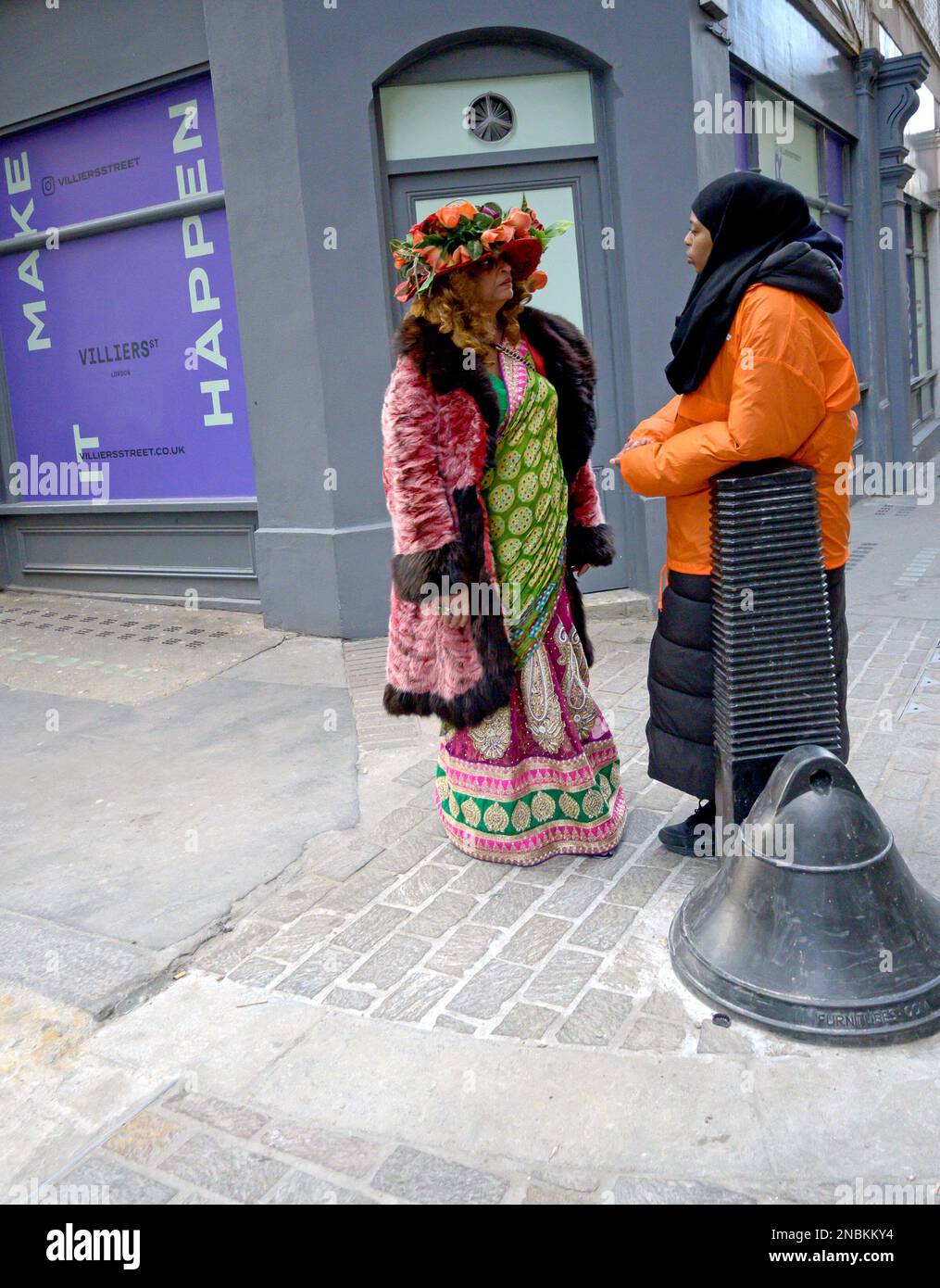 London, England, UK. A colourfully-dressed woman talking to a worker ...