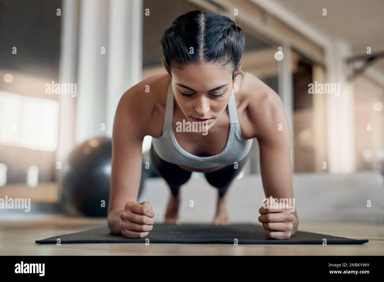 Powering through. Full length shot of an attractive young female athlete planking in the gym ...