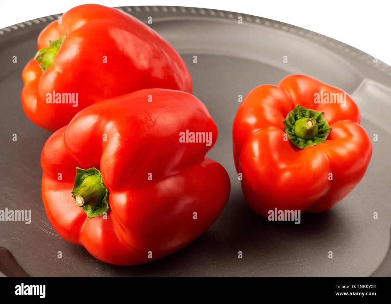 Three bright red paprikas on a black tray isolate on a white background ...