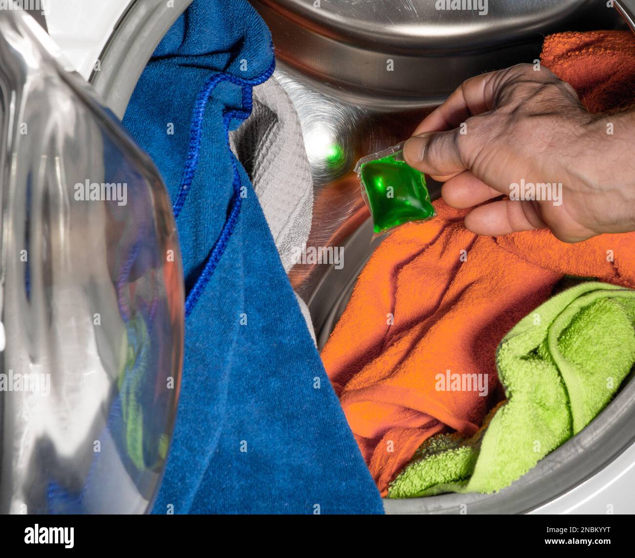 a hand puts a gel sachet of detergent into the washing machine Stock ...